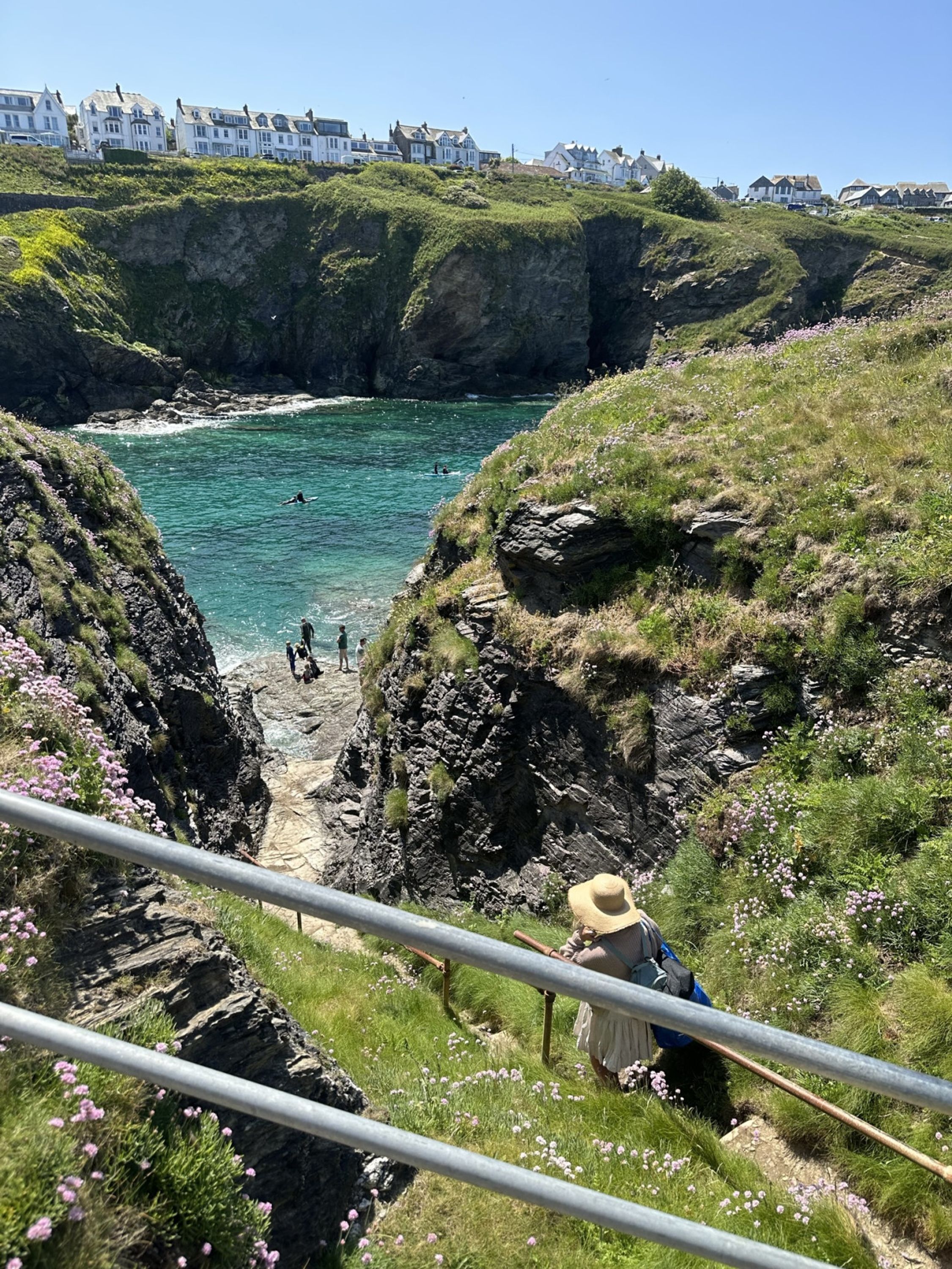 Um penhasco costeiro com uma trilha estreita que desce até o mar, com vista para uma fileira de casas.