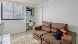 Uma sala de estar moderna com um sofá marrom, uma pequena escrivaninha branca e uma janela grande.