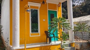 Um pequeno edifício térreo com fachada amarela, porta verde e varanda com uma cadeira.