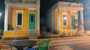 Dois edifícios amarelos com portas e janelas verdes, cada um com um pequeno alpendre e degraus até a entrada.