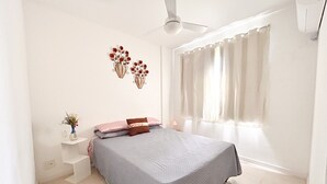 Um quarto com cama, mesa de cabeceira, luminária na parede e janela com cortinas.
