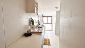 Corredor estreito com piso em azulejo e uma área de cozinha, incluindo pia, bancada e suporte suspenso.