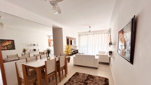 Uma sala de estar moderna com área de jantar, um tapete felpudo grande e uma TV fixada na parede.