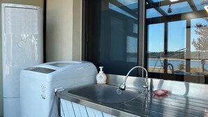 Um banheiro moderno com uma pia de aço inoxidável, um dispensador de toalhas branco e uma janela com vista para um edifício e árvores.