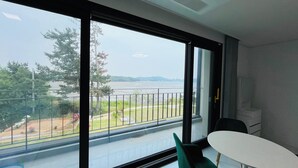 Quarto com uma grande porta de vidro deslizante que dá para uma varanda com vista para um rio e vegetação.
