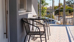 Varanda com mesa e cadeiras, janela e vista para a rua e árvores.
