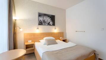Quarto de hotel com cama, mesas de cabeceira, uma mesinha e um quadro na parede.