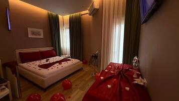 Quarto de hotel com uma cama, uma mesinha com toalha vermelha e uma televisão na parede.