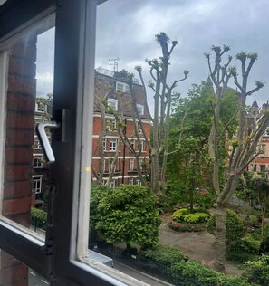 Vista de dentro de um edifício, mostrando uma fileira de casas de tijolos vermelhos com molduras de janelas brancas, cercadas por vegetação e árvores.
