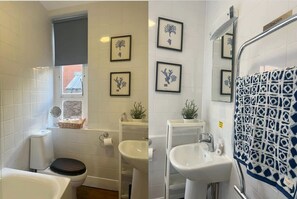 Casa de banho com sanita, lavatório e banheira. Existem quadros nas paredes e um porta-toalhas com uma toalha estampada.