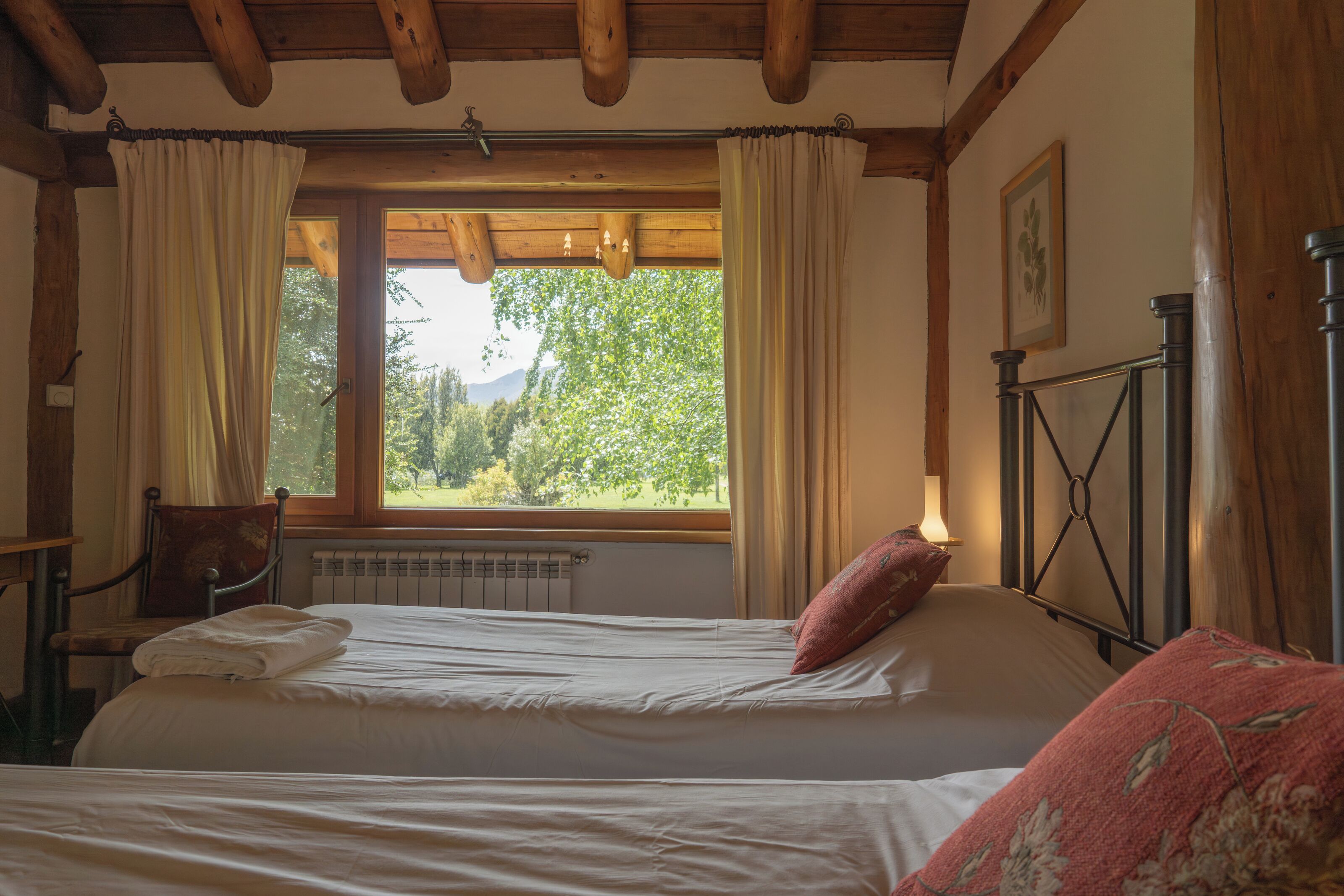 Quarto com cama grande, janela com cortinas, radiador e teto de madeira.