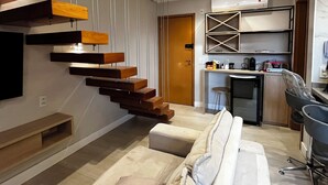 Sala moderna com escada, sofá e área de cozinha.