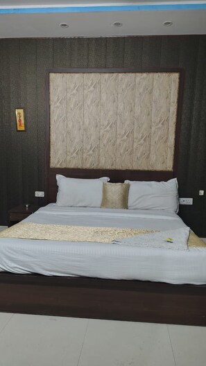 Quarto com cama grande, cabeceira de madeira escura e uma mesinha de cabeceira.