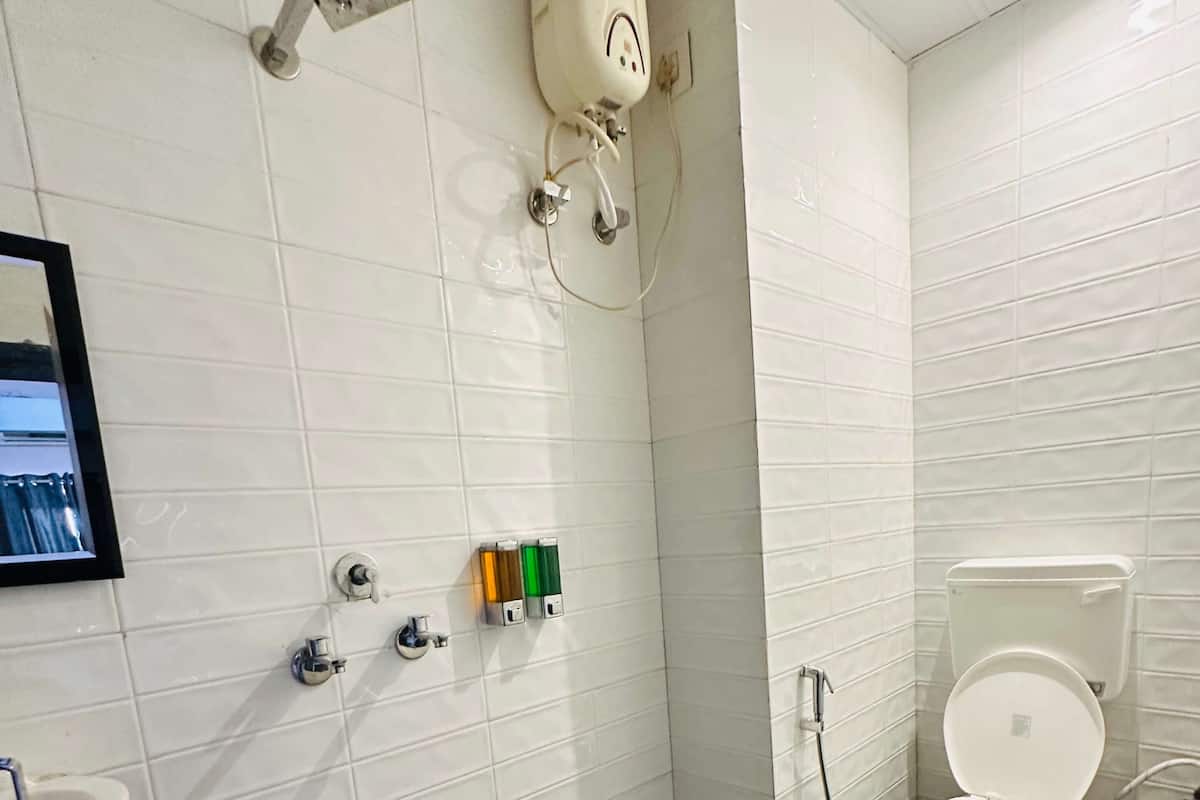 Casa de banho com sanita, lavatório e chuveiro. Existem dispensadores de sabonete e um suporte para papel higiénico na parede.