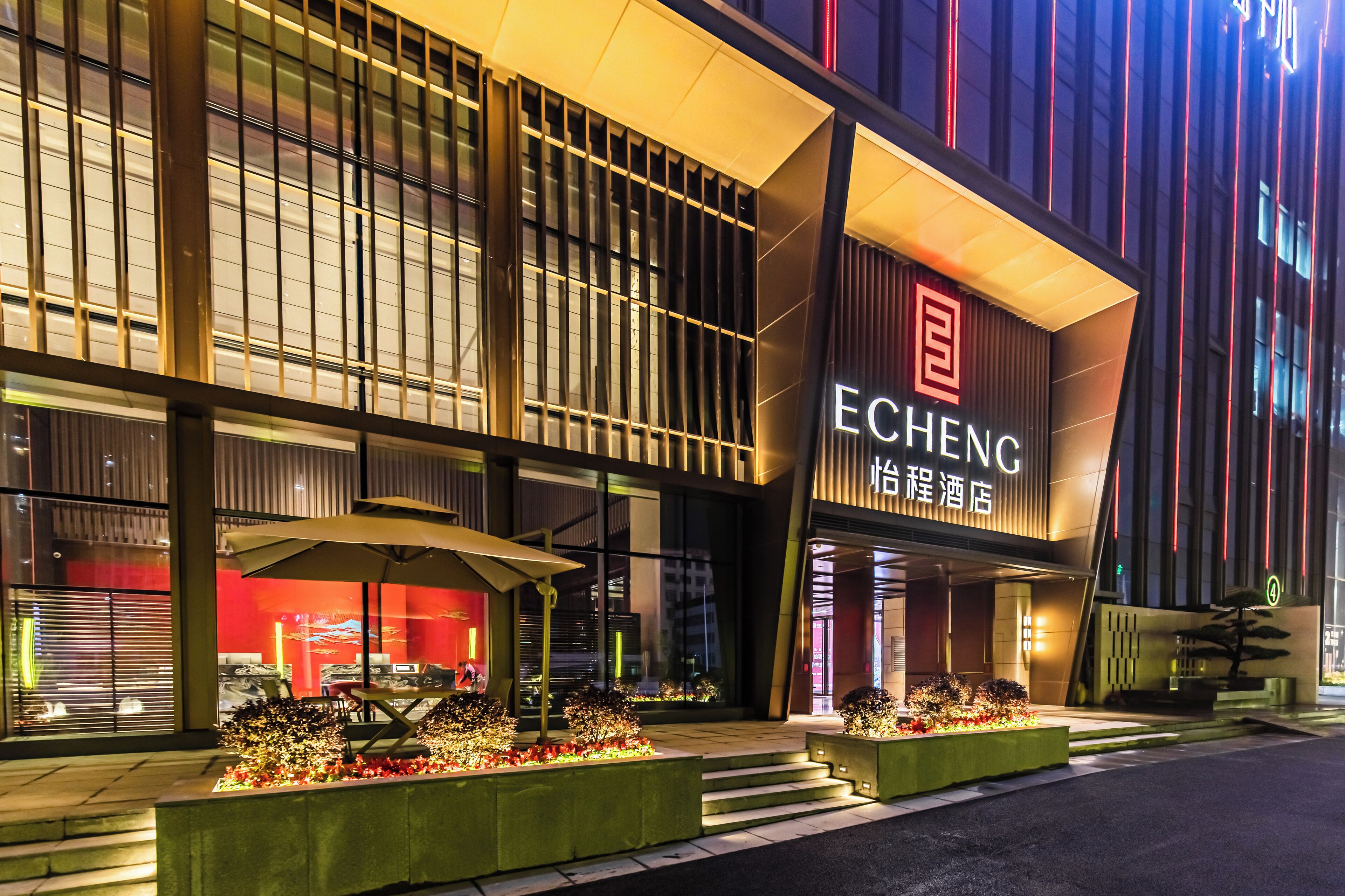 Um hotel moderno com uma placa chamativa com a inscrição "ECHENG" e uma área de entrada bem iluminada com mesas ao ar livre.