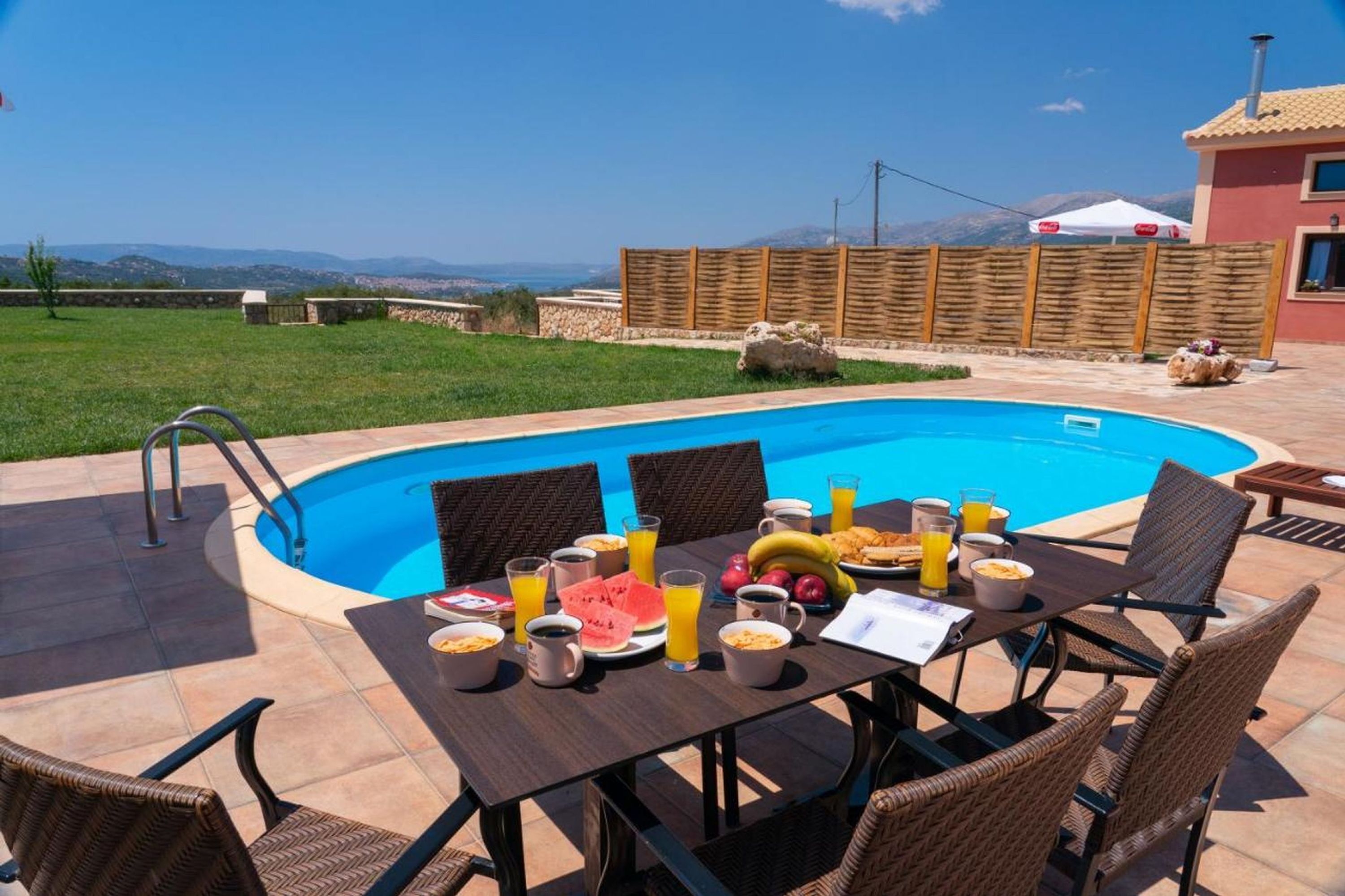 Disposição para café da manhã à beira da piscina, com mesa, cadeiras e vista para a piscina e paisagem.