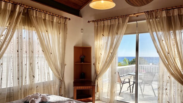 Quarto de hotel com cama, prateleira de madeira com um vaso e varanda com vista para o mar.