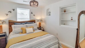 Quarto com cama, abajures, espelho e enfeites na parede.