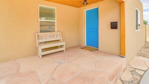 Varanda coberta com uma porta azul, um banco de madeira e uma prateleira pequena.