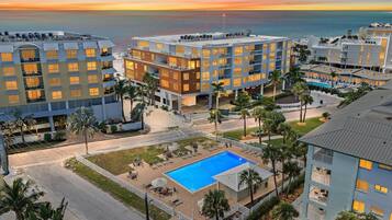 Hotel com vários edifícios, piscina e vista para o oceano ao pôr do sol.