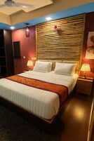 Quarto de hotel com uma cama grande, duas luminárias de cabeceira, um ventilador de teto e um painel de cabeceira de madeira.