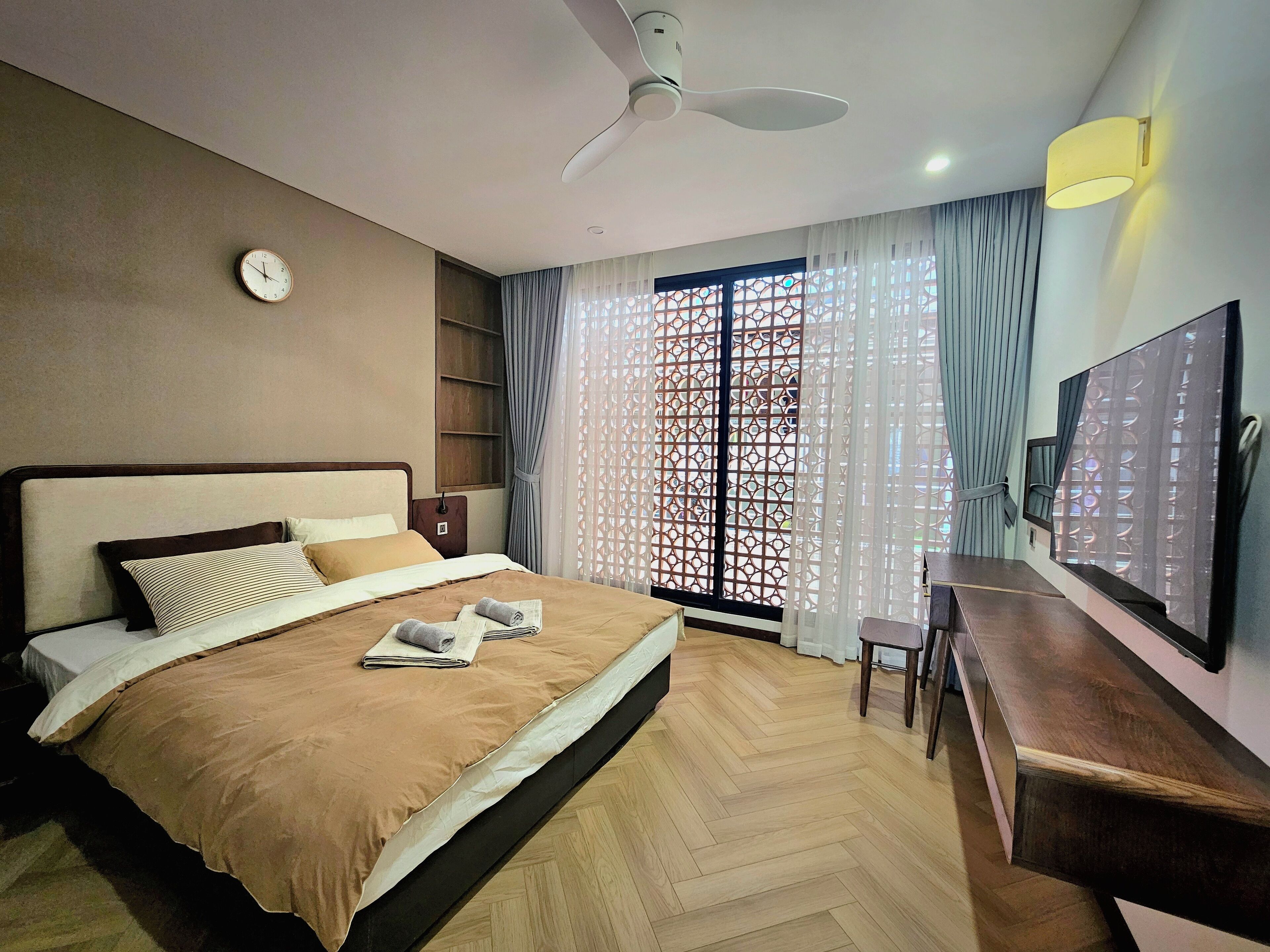 Quarto de hotel moderno com uma cama grande, uma escrivaninha, uma televisão e um ventilador de teto.
