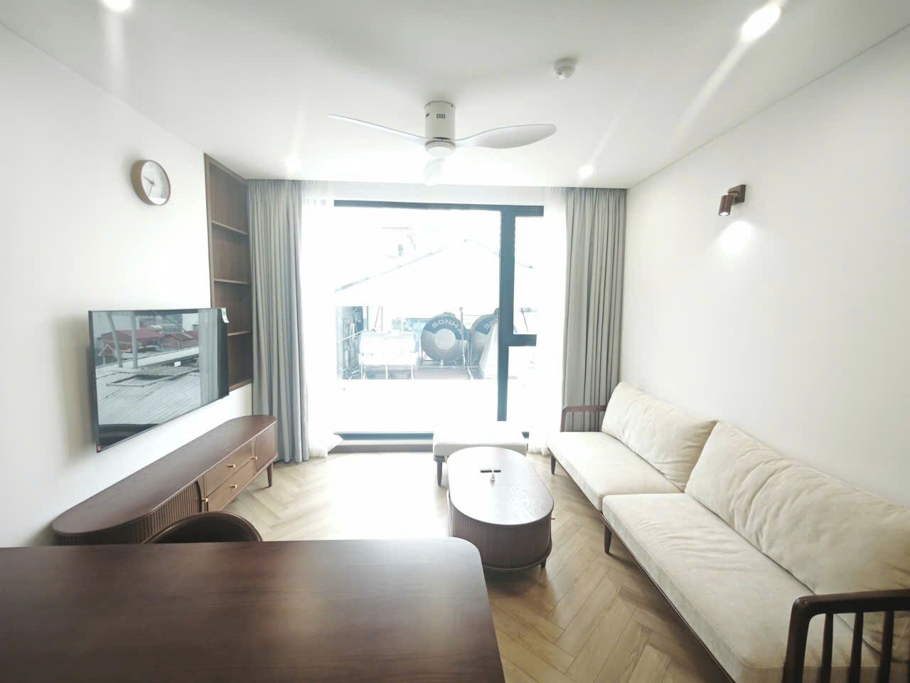 Uma sala de estar moderna com um sofá, uma mesa de centro, uma televisão sobre um suporte e um ventilador de teto.