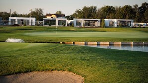 Um campo de golfe com edifícios modernos, um lago e um bunker de areia.