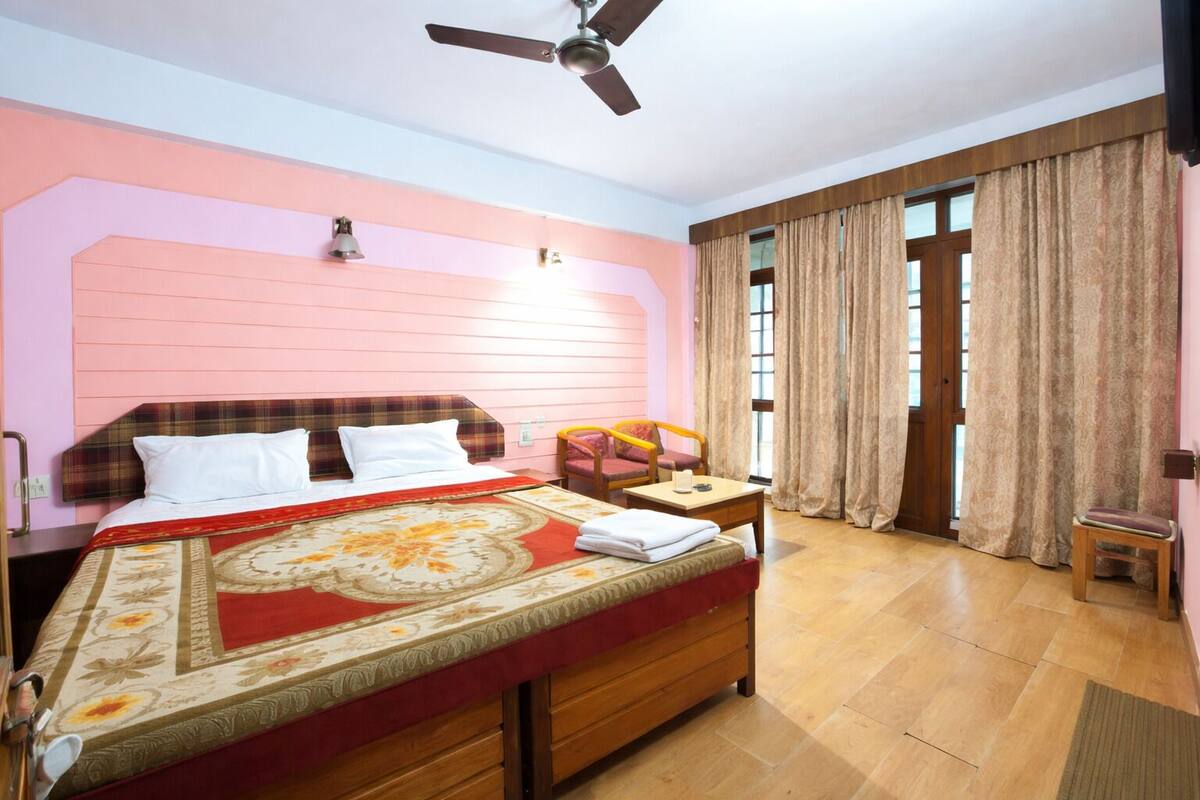 Quarto com cama, cadeira, mesa, ventoinha no teto e janela com cortinas.