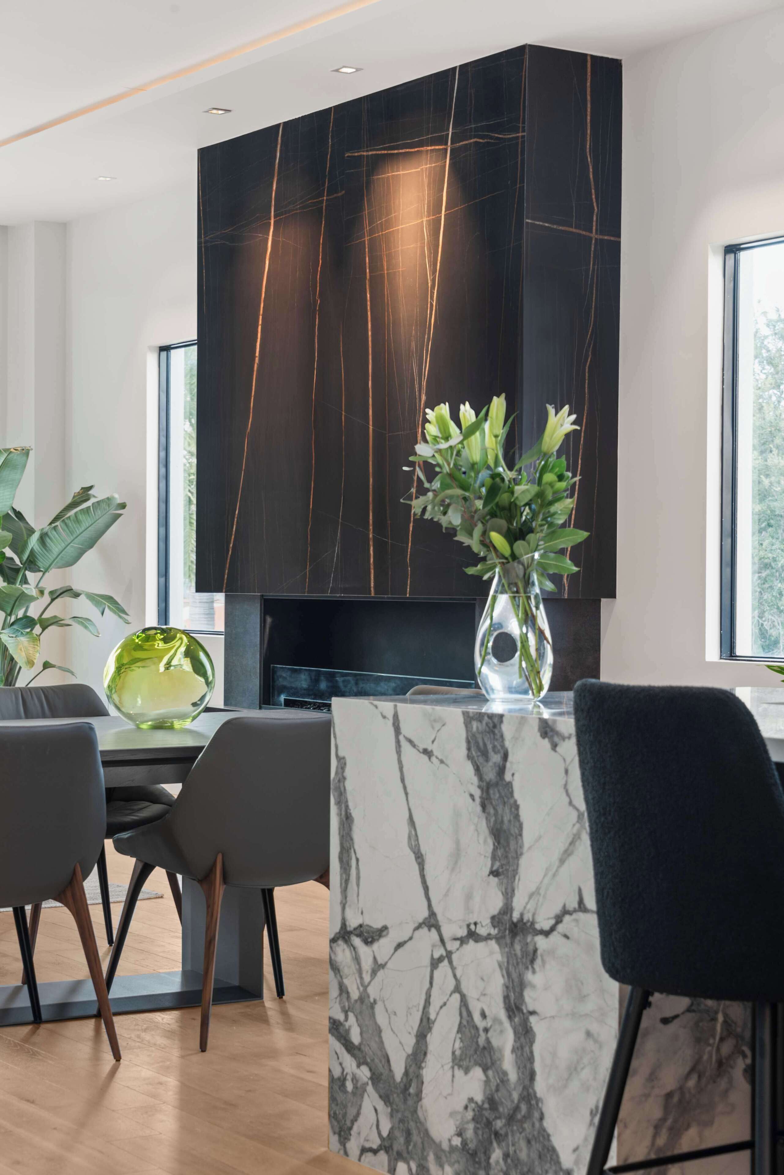 Cozinha moderna com painel de mármore preto, um vaso de vidro com plantas verdes e bancada de mármore.