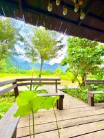 Um deck de madeira com bancos oferece vista para uma paisagem verdejante, com árvores e montanhas.