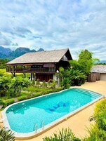 Piscina com deck de madeira e casa com telhado de palha.