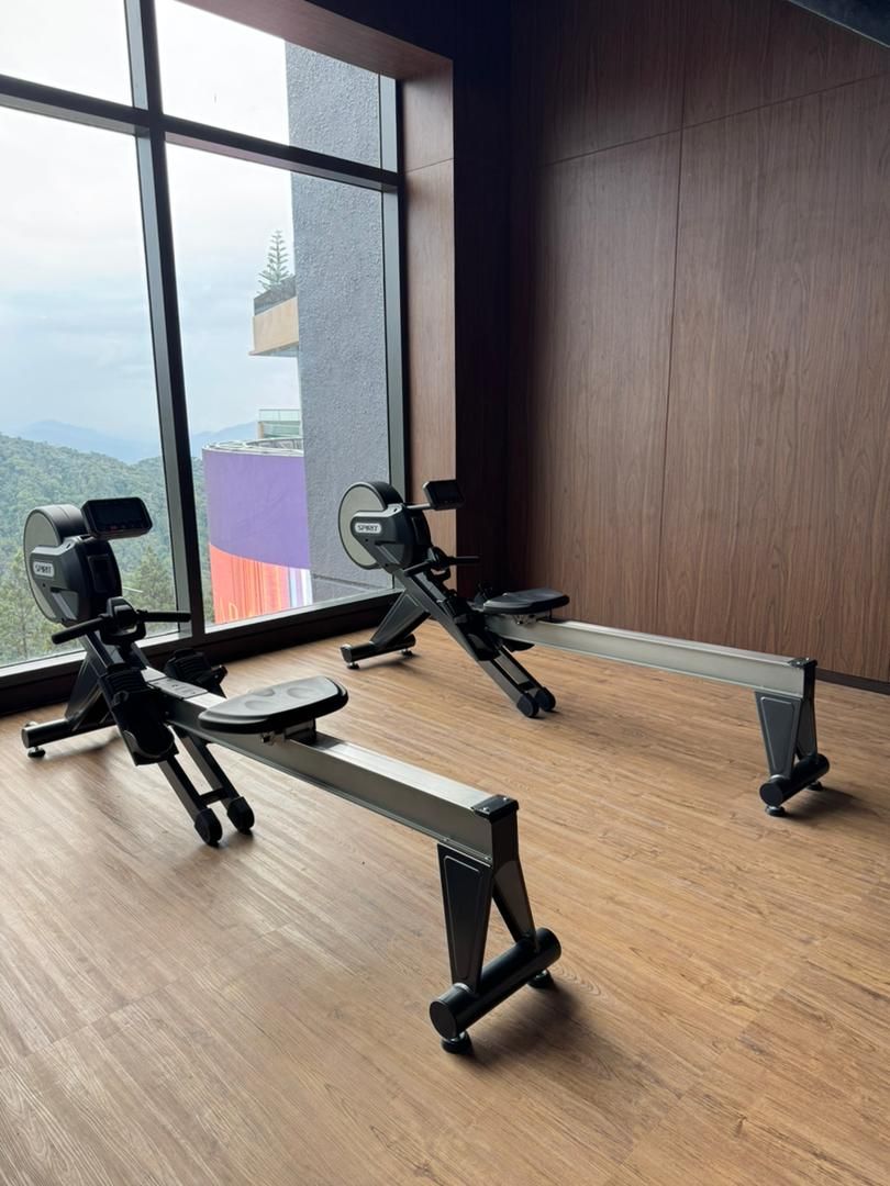 Uma academia com equipamentos de ginástica, janelas amplas e vista para uma montanha.