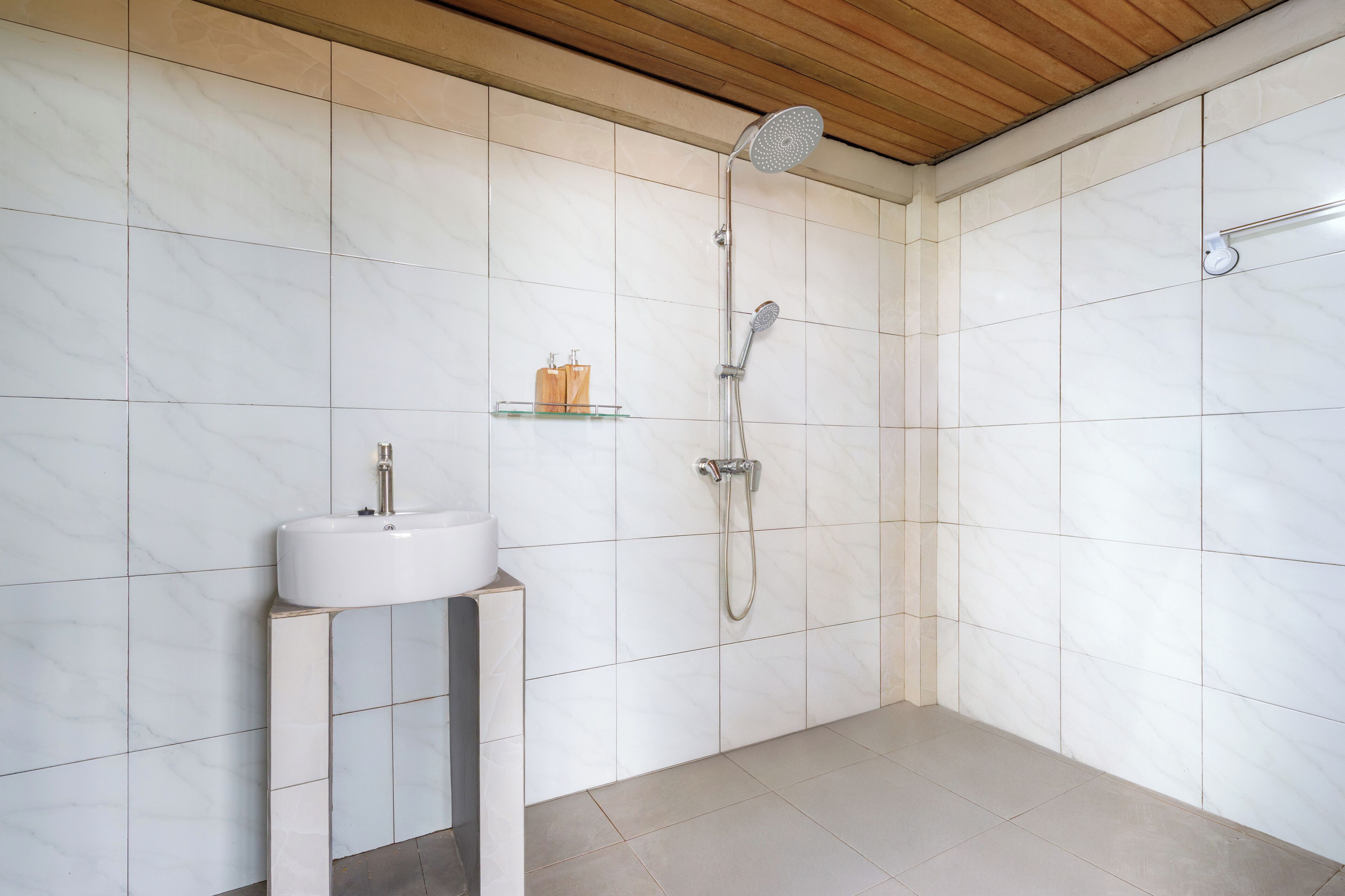 Casa de banho moderna com chuveiro, lavatório e prateleira de vidro com artigos de higiene pessoal.