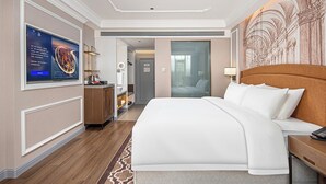 Quarto de hotel com uma cama grande, televisão fixada na parede, cómoda de madeira e casa de banho visível através de uma porta aberta.