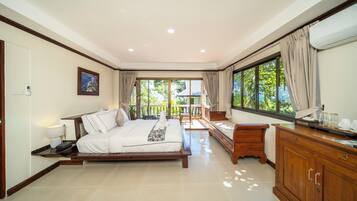 Um quarto espaçoso com uma cama grande, uma mesa de cabeceira de madeira, um aparador de madeira e vista para o exterior por grandes janelas.