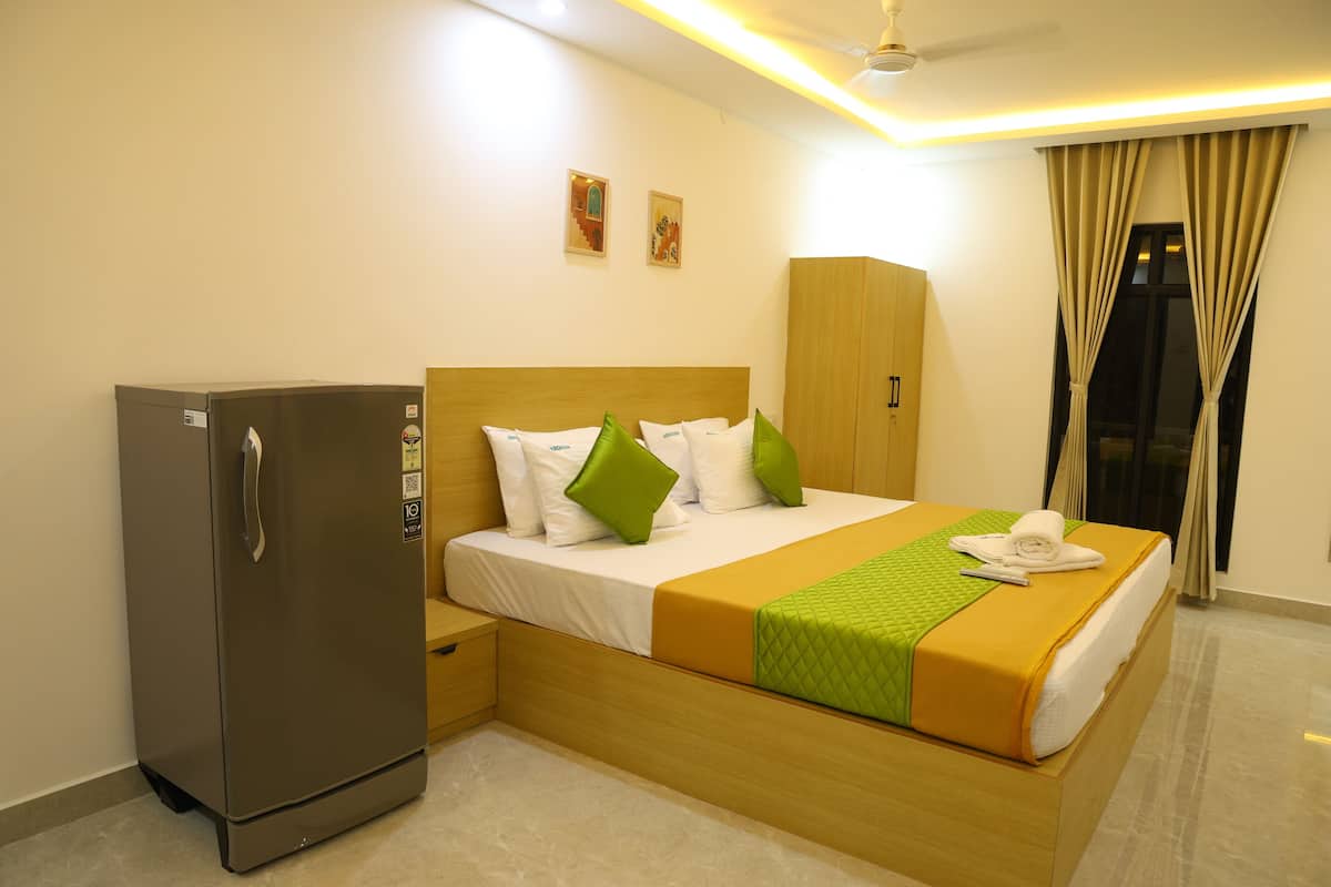 Quarto de hotel com cama, guarda-roupa, frigorífico e janela com cortinas.