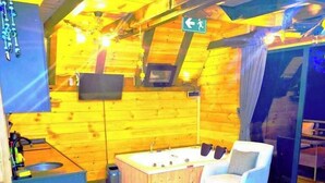 Interior acolhedor de uma cabana de madeira com piso de madeira, um sofá branco, um banco de madeira, uma mesinha e uma janela grande.
