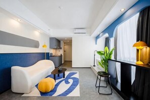 Um saguão de hotel moderno com um sofá, uma mesinha, uma planta e vista para a área da cozinha.