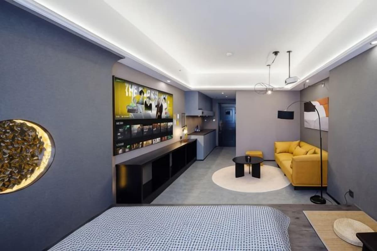 Quarto de hotel moderno com cama, televisão, sofá e área de jantar.