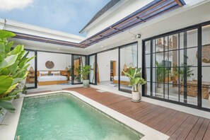 Quarto de hotel moderno com uma grande porta de vidro, deck de madeira, piscina e cama com vista para o exterior.