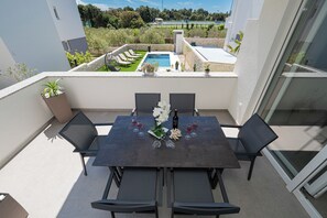 Varanda com mesa posta para dois, planta em vaso e vista para piscina e jardim.