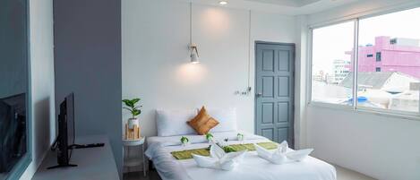 Quarto de hotel moderno com cama, televisão, janela com vista para a cidade e porta.