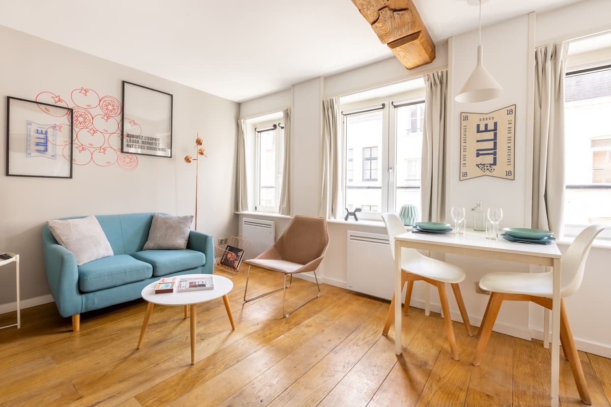 Uma sala de estar moderna com um sofá azul, uma mesa de centro redonda e um espaço de jantar com uma mesa e cadeiras brancas.