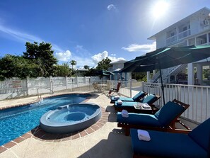 Uma área de piscina com hidromassagem, espreguiçadeiras e guarda-sóis.