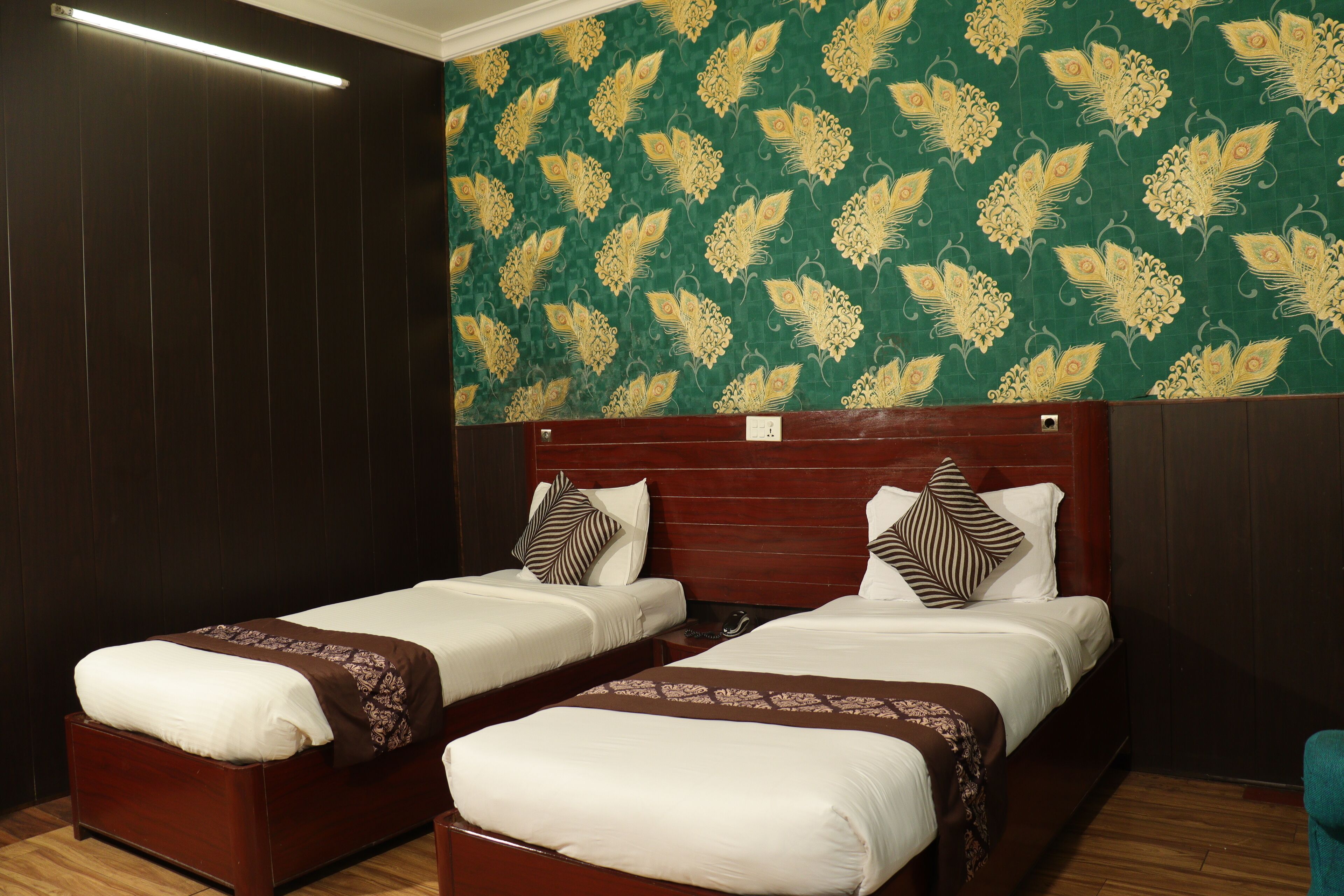 Quarto de hotel com duas camas de solteiro, cabeceira de madeira e papel de parede floral verde.