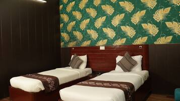 Quarto de hotel com duas camas de solteiro, cabeceira de madeira e papel de parede floral verde.