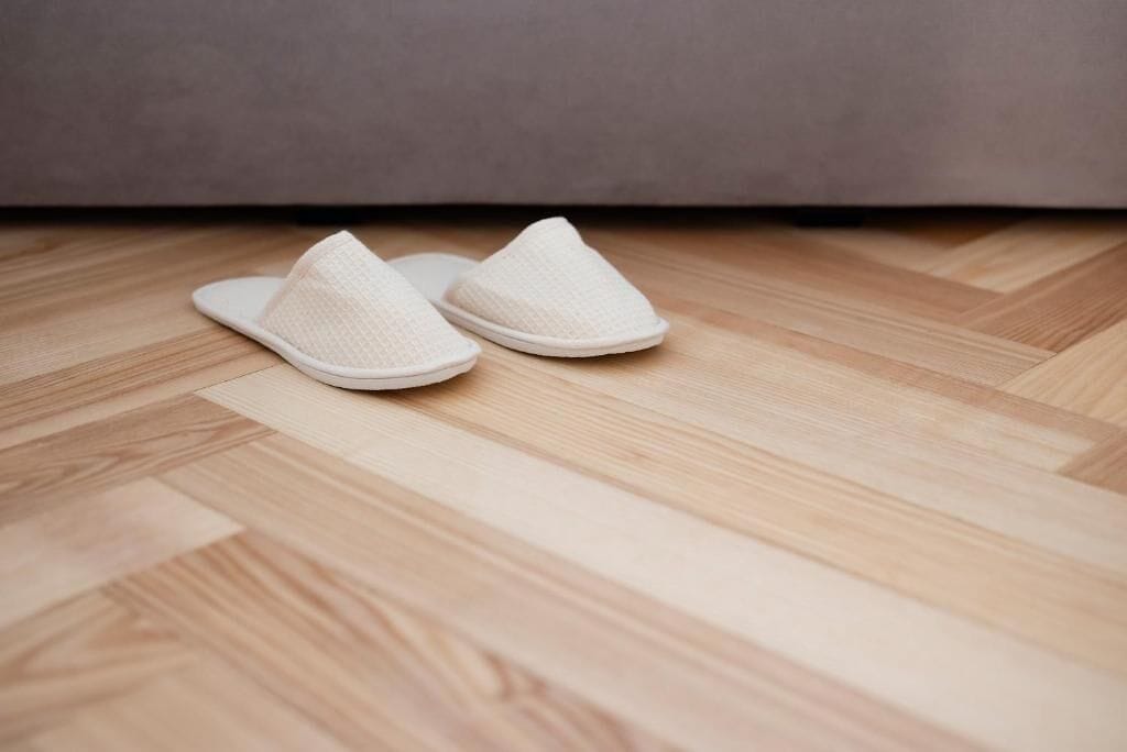 Um par de sapatos brancos tipo slip-on sobre um piso de madeira.