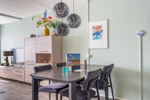 Uma sala de jantar moderna com um armário de madeira, uma mesa e cadeiras. Há um vaso com flores no armário e uma moldura com uma fotografia na parede.