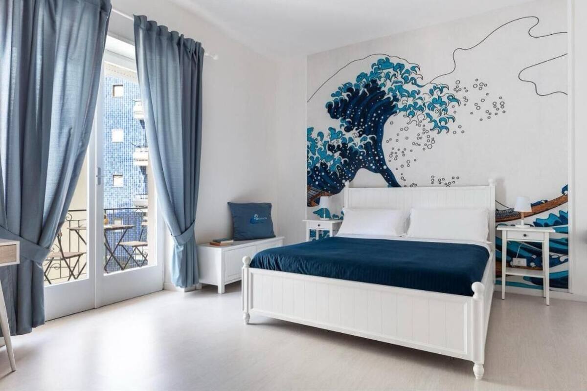 Quarto com cama branca, um mural grande na parede e vista para a varanda externa.